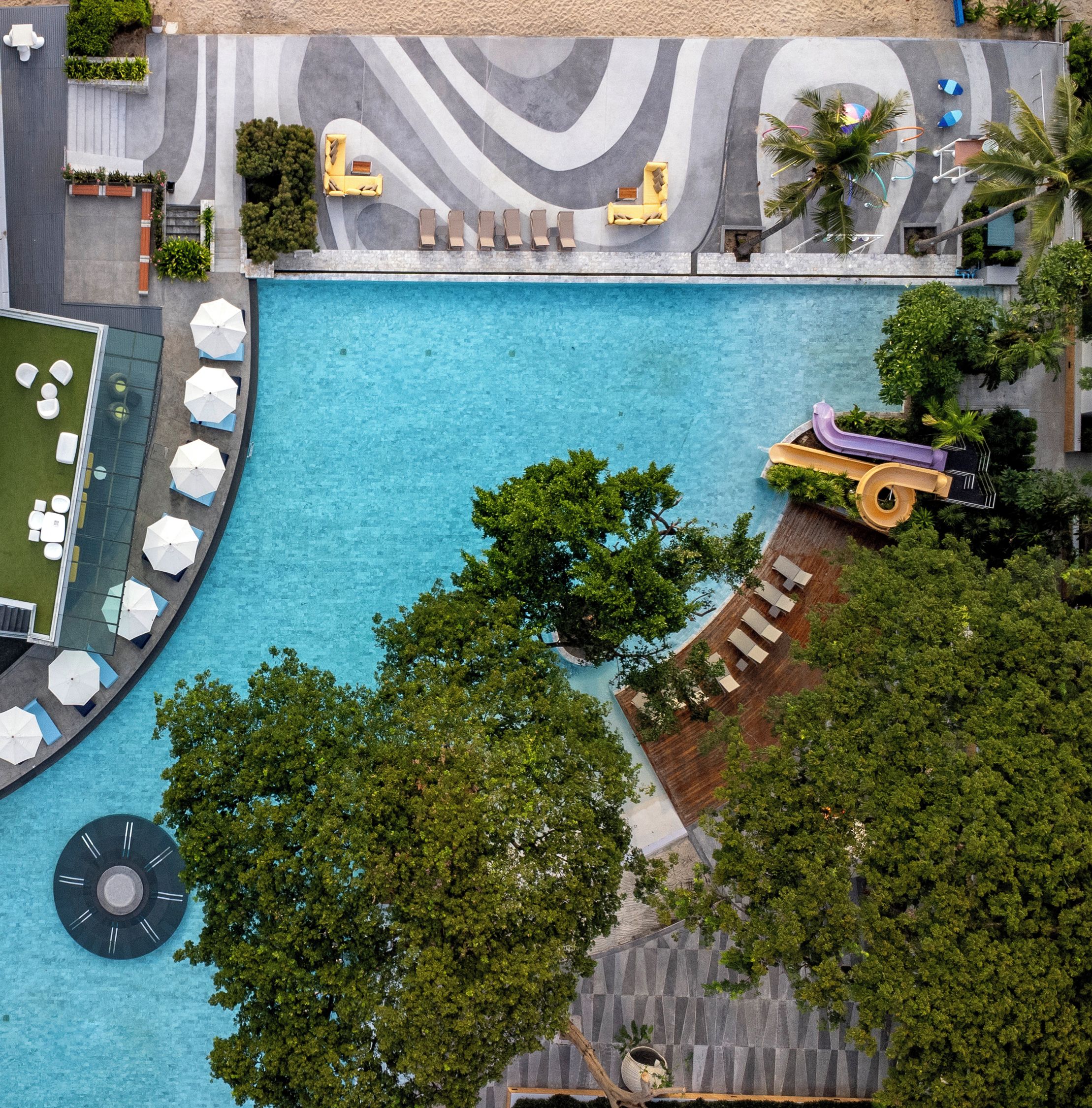Vista aérea de um resort com uma grande piscina, espreguiçadeiras e um deque de madeira.