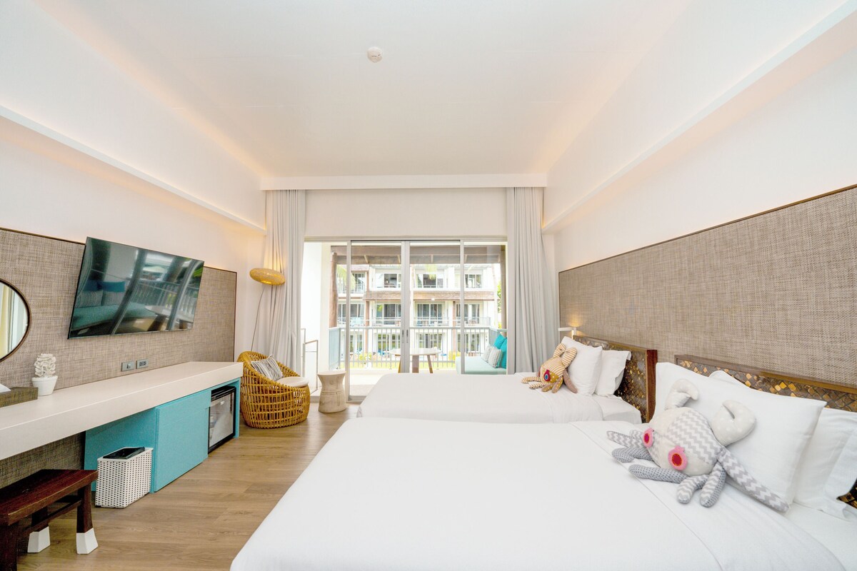 Quarto de hotel com uma cama grande, uma TV na parede, uma cadeira de vime e vista para o exterior do edifício.