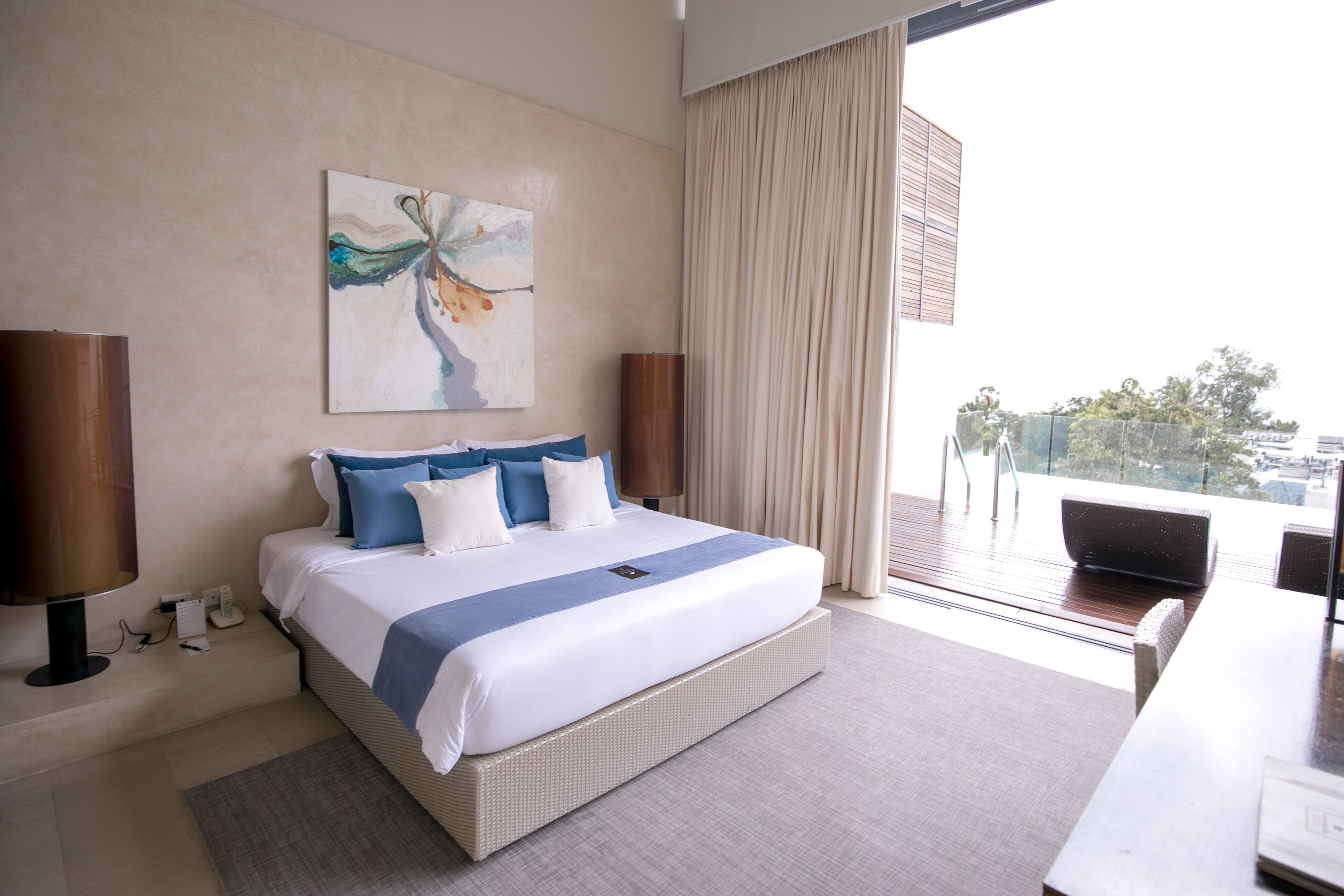 Quarto de hotel moderno com uma cama grande, vista para a cidade e varanda com mesa e cadeiras.