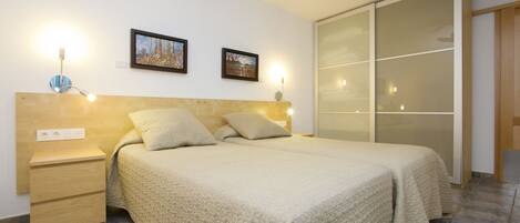 Quarto com cama, mesas de cabeceira, luminárias fixadas na parede e um armário com porta de vidro deslizante.