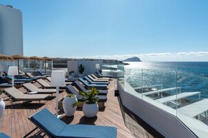 Terraço com espreguiçadeiras e plantas em vasos, com vista para a costa.