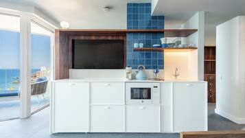 Cozinha moderna com televisão grande, forno embutido e vista para o mar.