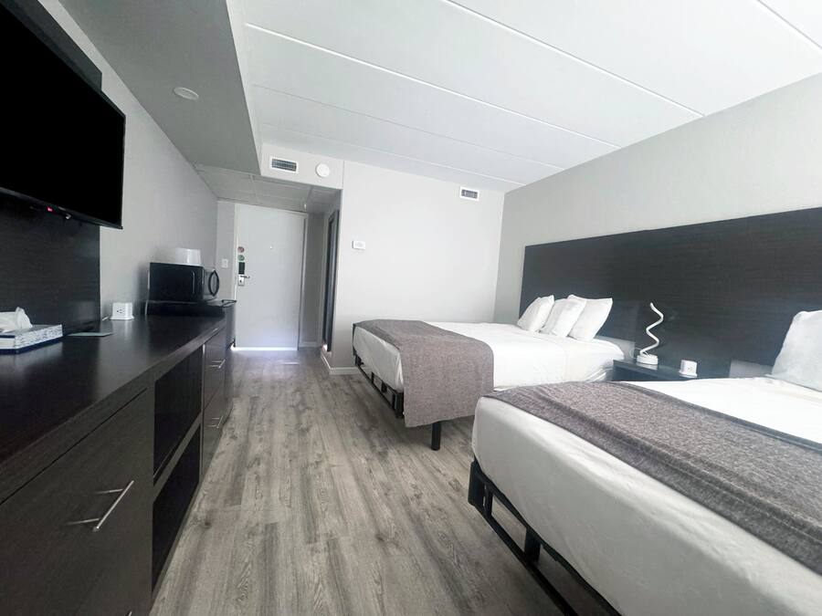 Quarto de hotel com duas camas, uma televisão de tela plana, uma mesa com micro-ondas e uma porta que dá para outro cômodo.