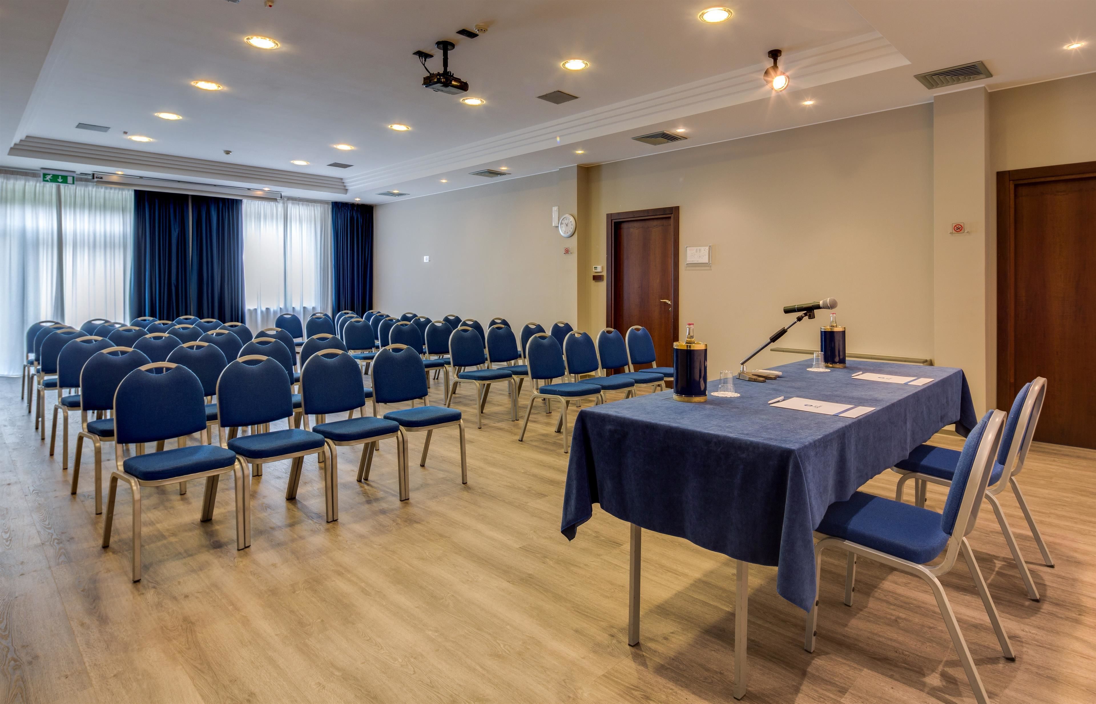 Uma sala de conferências com fileiras de cadeiras azuis e uma mesa coberta por um tecido azul.