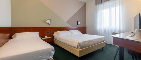 Quarto de hotel com duas camas, uma escrivaninha, uma cadeira, uma televisão e janela com cortinas.