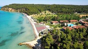 Vista aérea de um hotel à beira-mar, com praia, piscina e floresta ao redor.