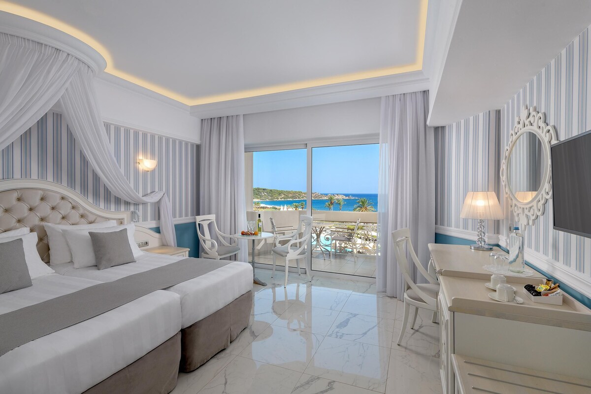Um quarto luxuoso com uma cama grande, um espaço de estar com vista para o mar e uma varanda com mobiliário de exterior.