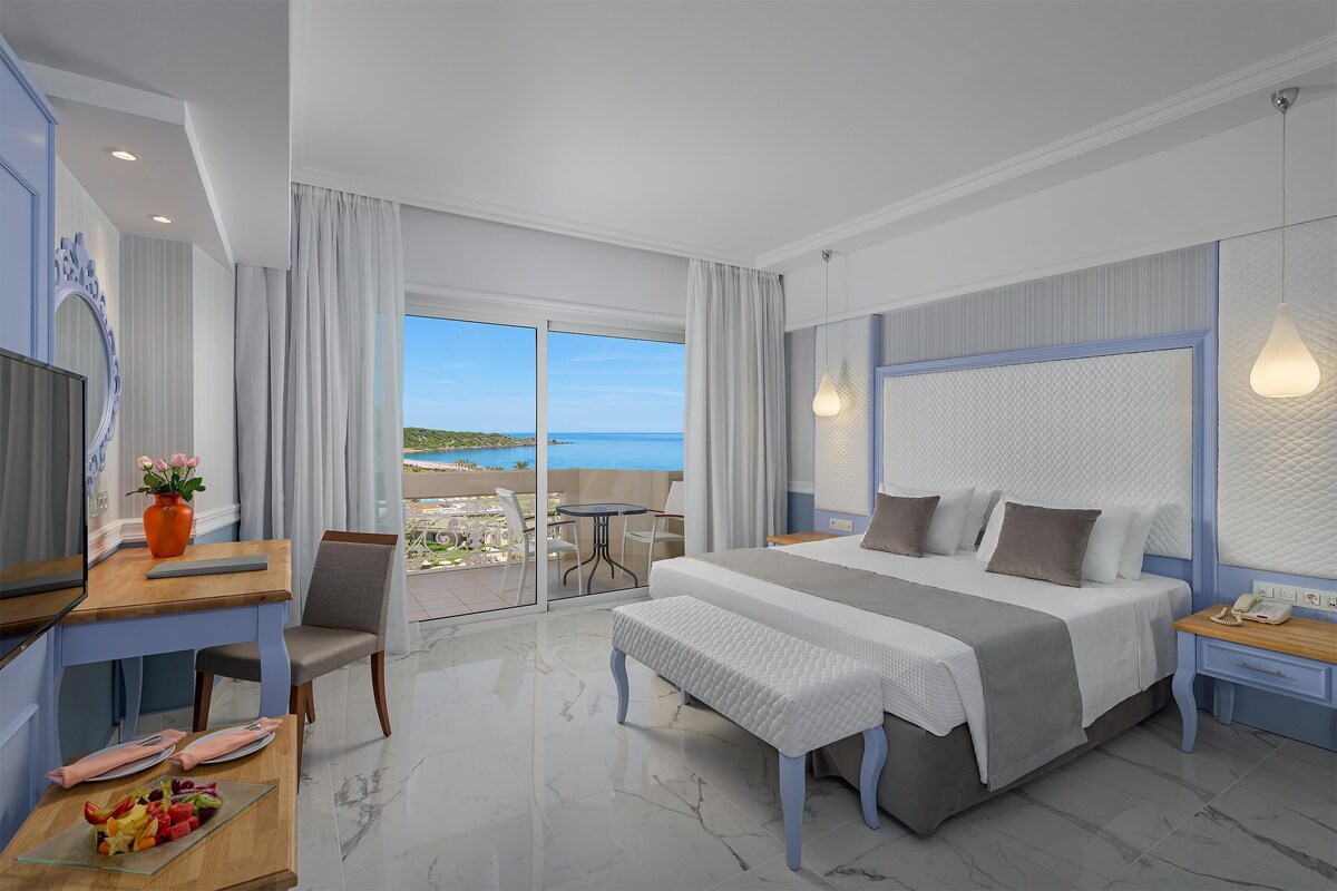 Quarto de hotel moderno com uma cama grande, uma escrivaninha e varanda com vista para o mar.