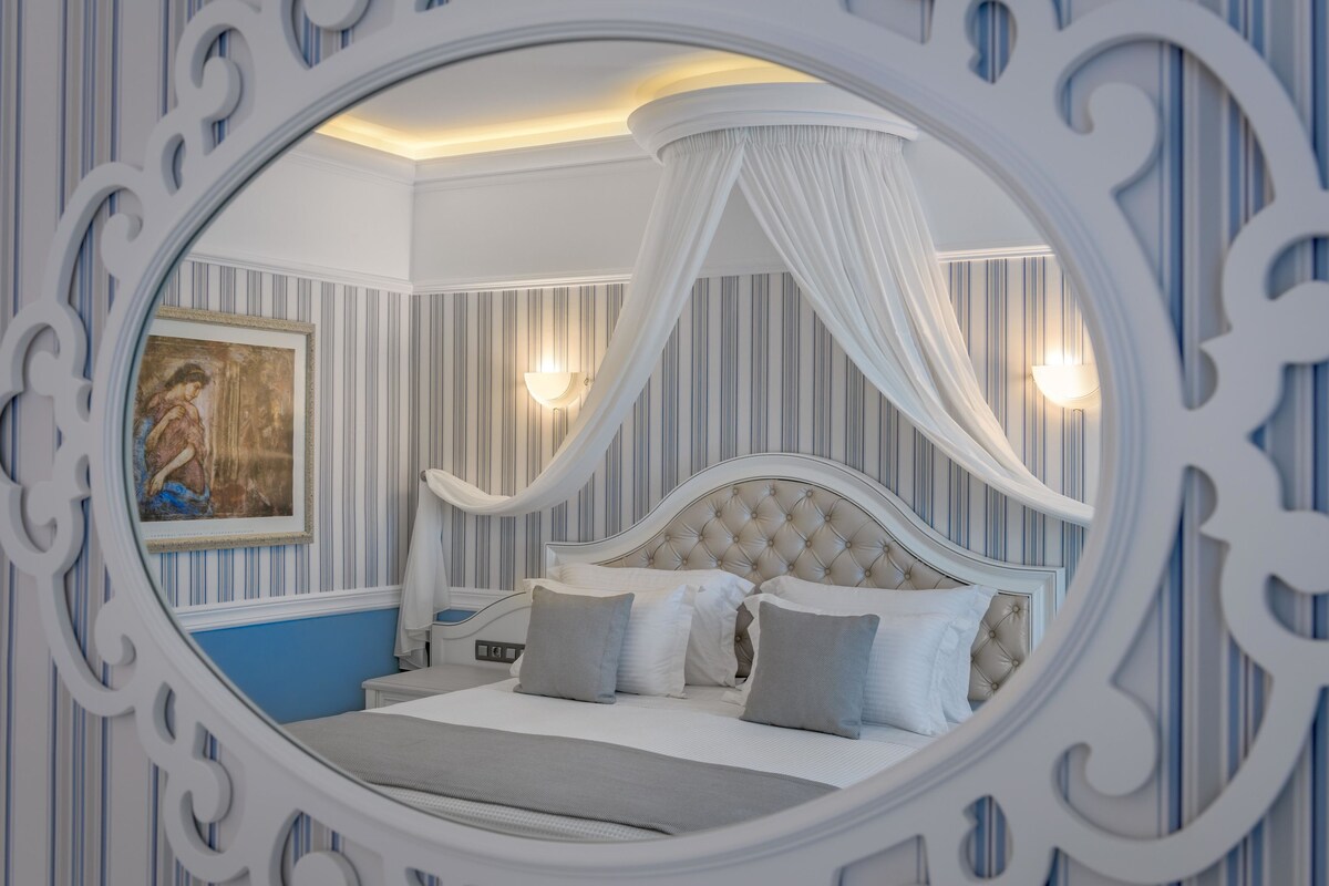 Quarto com cabeceira estofada, cama de dossel, papel de parede listrado e um quadro na parede.