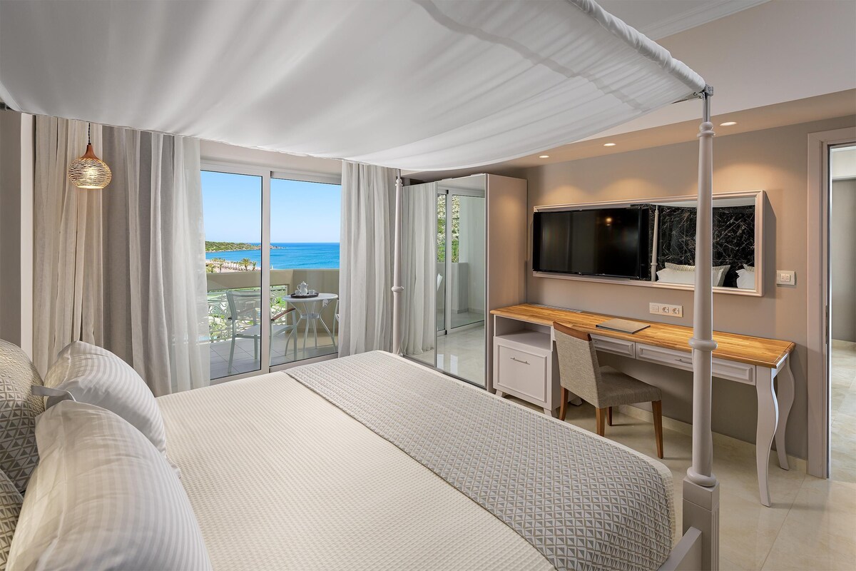 Quarto com cama, escrivaninha, televisão e varanda com vista para o mar.
