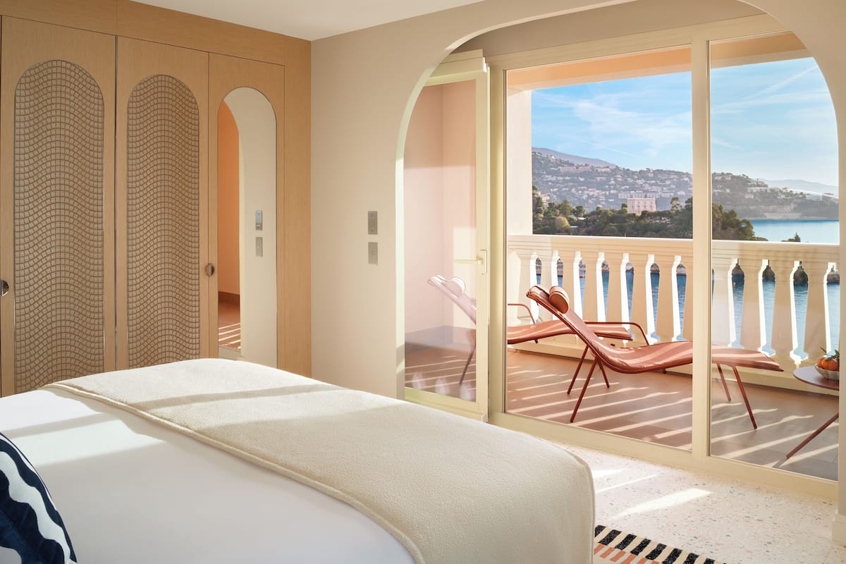Quarto com cama grande, varanda com vista para o mar e porta de correr com padrão decorativo.