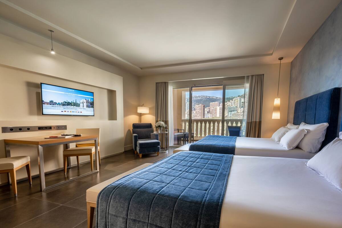 Quarto de hotel com duas camas, uma escrivaninha, uma cadeira e uma televisão.