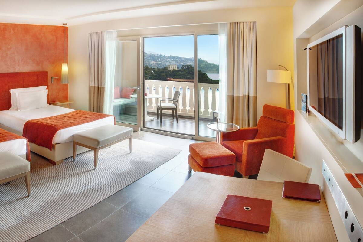 Quarto de hotel com duas camas, varanda e vista, uma mesa e uma cadeira.
