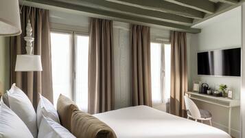 Quarto de hotel com cama, escrivaninha, cadeira, televisão e cortinas.