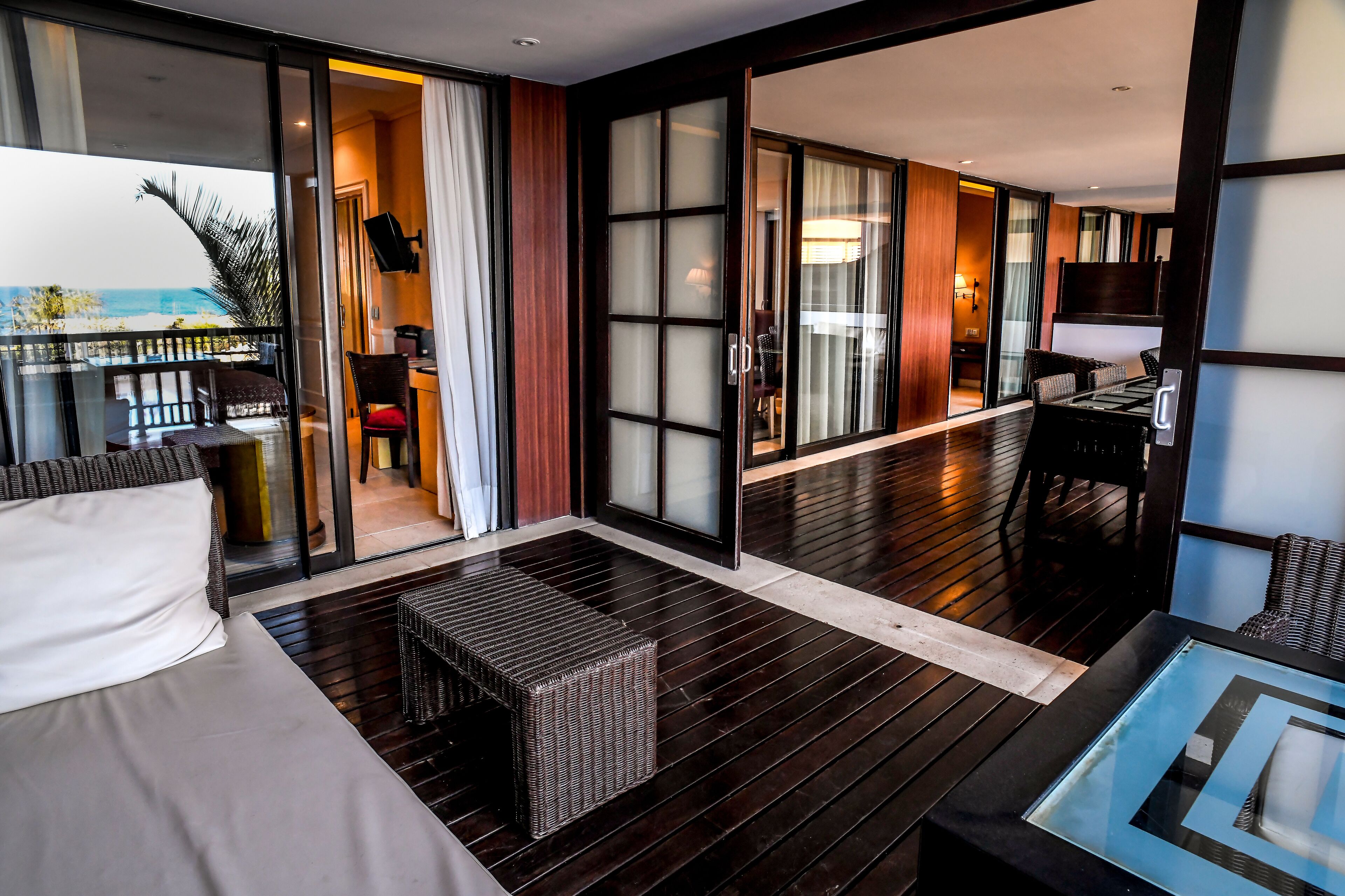 Quarto de hotel moderno com uma grande porta de vidro deslizante para uma varanda, uma cama com vista e uma pequena área de estar com uma mesa.