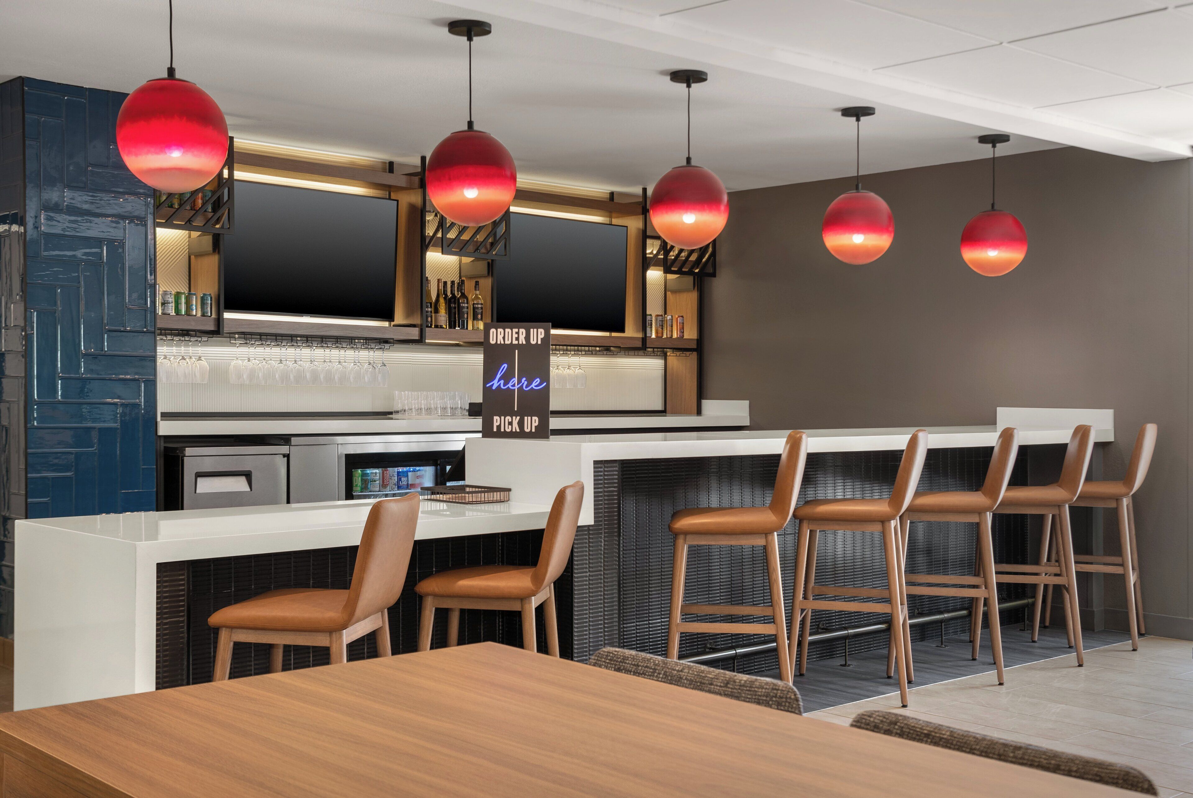 Uma área de bar moderna, com balcão, banquetas e luminárias pendentes vermelhas.