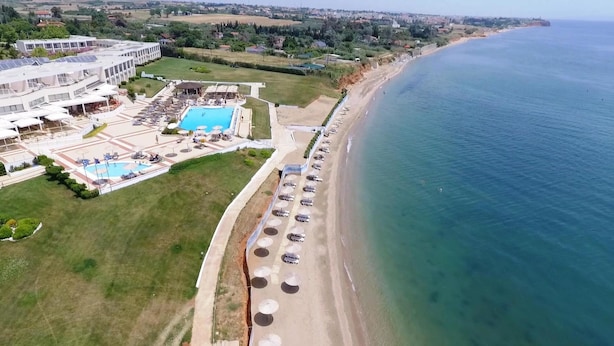Vista aérea de um resort à beira-mar com piscina, guarda-sóis e uma extensa faixa de areia.