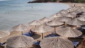 Uma praia com guarda-sóis de palha e espreguiçadeiras.