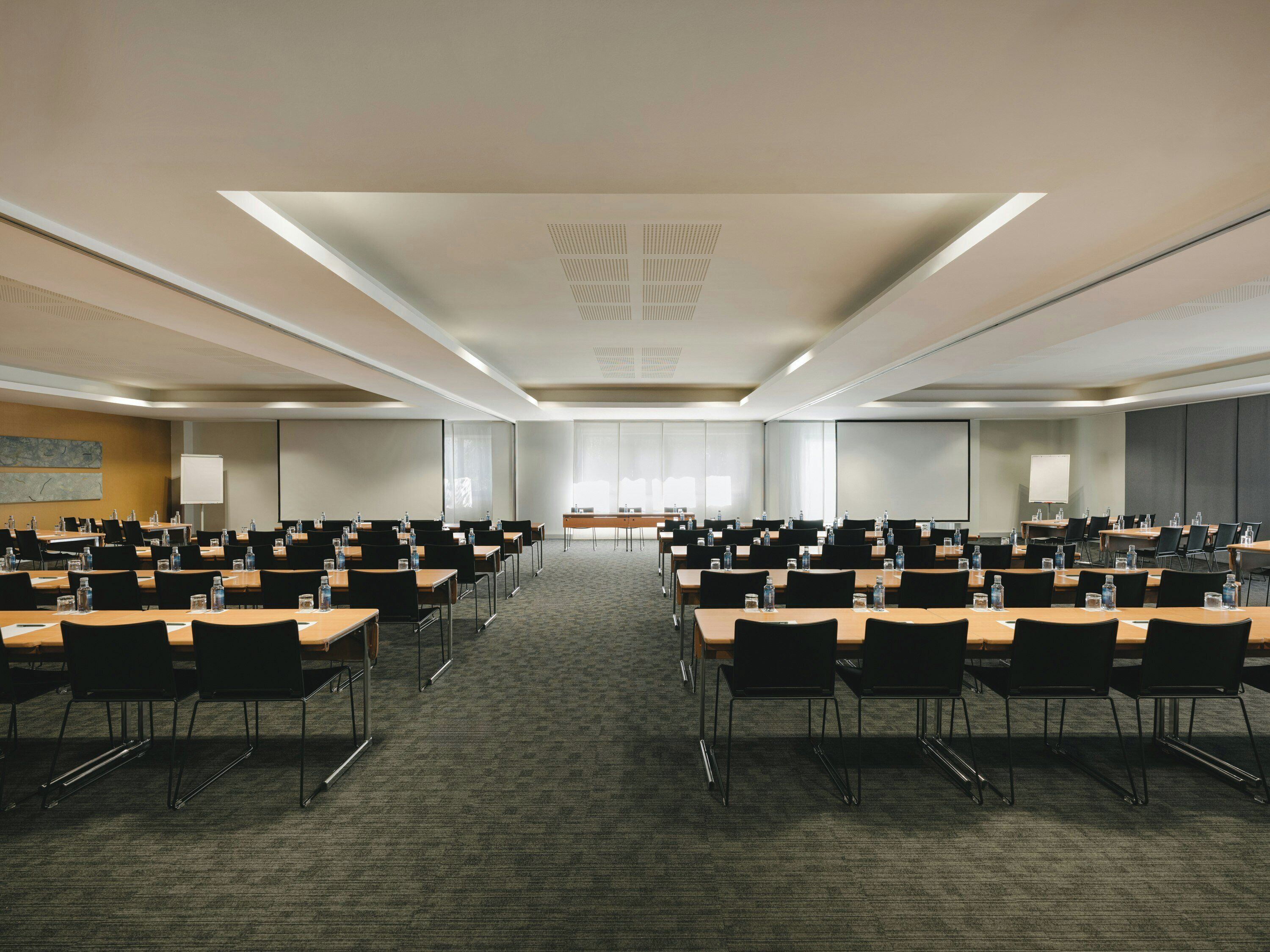 Uma sala de conferências com várias mesas e cadeiras, uma tela grande e uma lousa.
