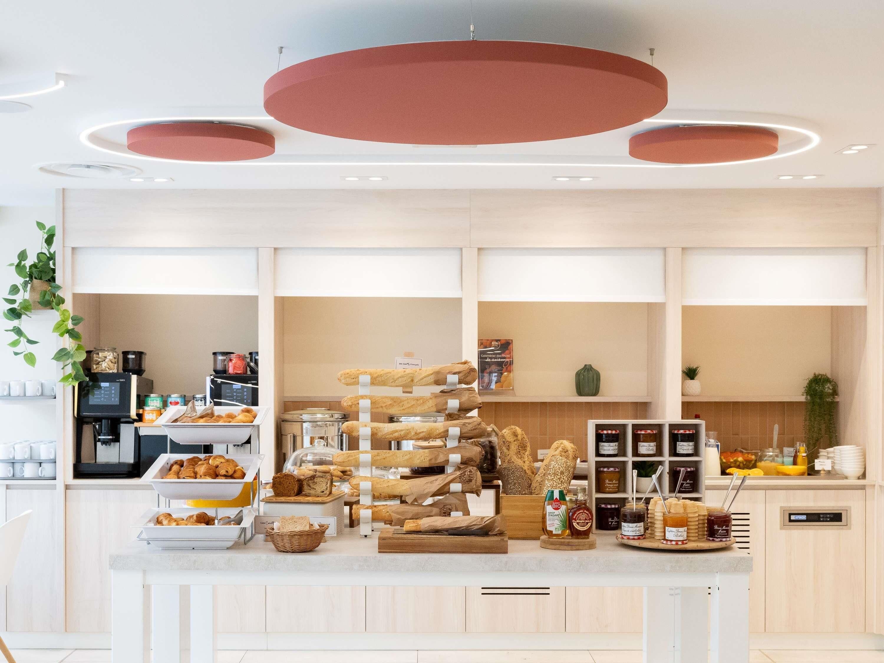 Balcão de padaria com diversos pães e doces, uma máquina de café e um visor digital.