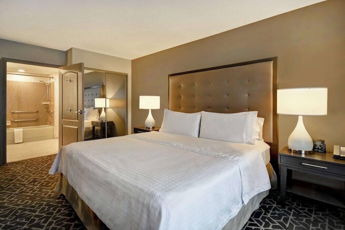 Quarto de hotel com cama grande, duas luminárias de cabeceira, mesa de cabeceira e banheiro com banheira e chuveiro.