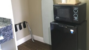 Uma cozinha compacta equipada com micro-ondas e frigorífico, uma tábua de passar pequena e um espaço para sapatos.