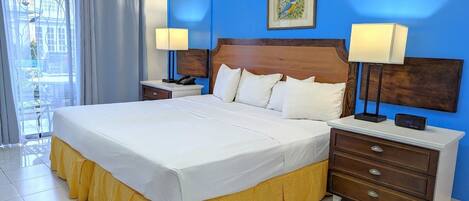 Quarto de hotel com uma cama grande, duas mesas de cabeceira, um criado-mudo, ar condicionado fixado na parede e uma janela com cortinas.