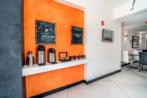 Uma área de recepção com parede de destaque laranja, um espaço para café e quadros-negros com o menu.