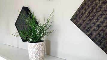 Uma planta em vaso, com um vaso de padrão geométrico, colocada sobre uma superfície branca, em frente a uma parede com painéis decorativos.