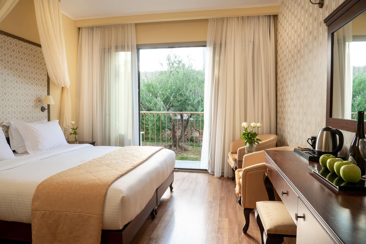 Quarto de hotel com uma cama grande, uma escrivaninha com cafeteira e vista para o verde pela janela.