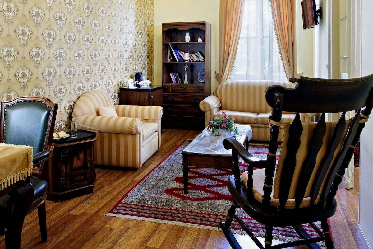 Uma sala de estar tradicional com piso de madeira, um sofá listrado, uma poltrona de balanço, uma estante e um lustre.