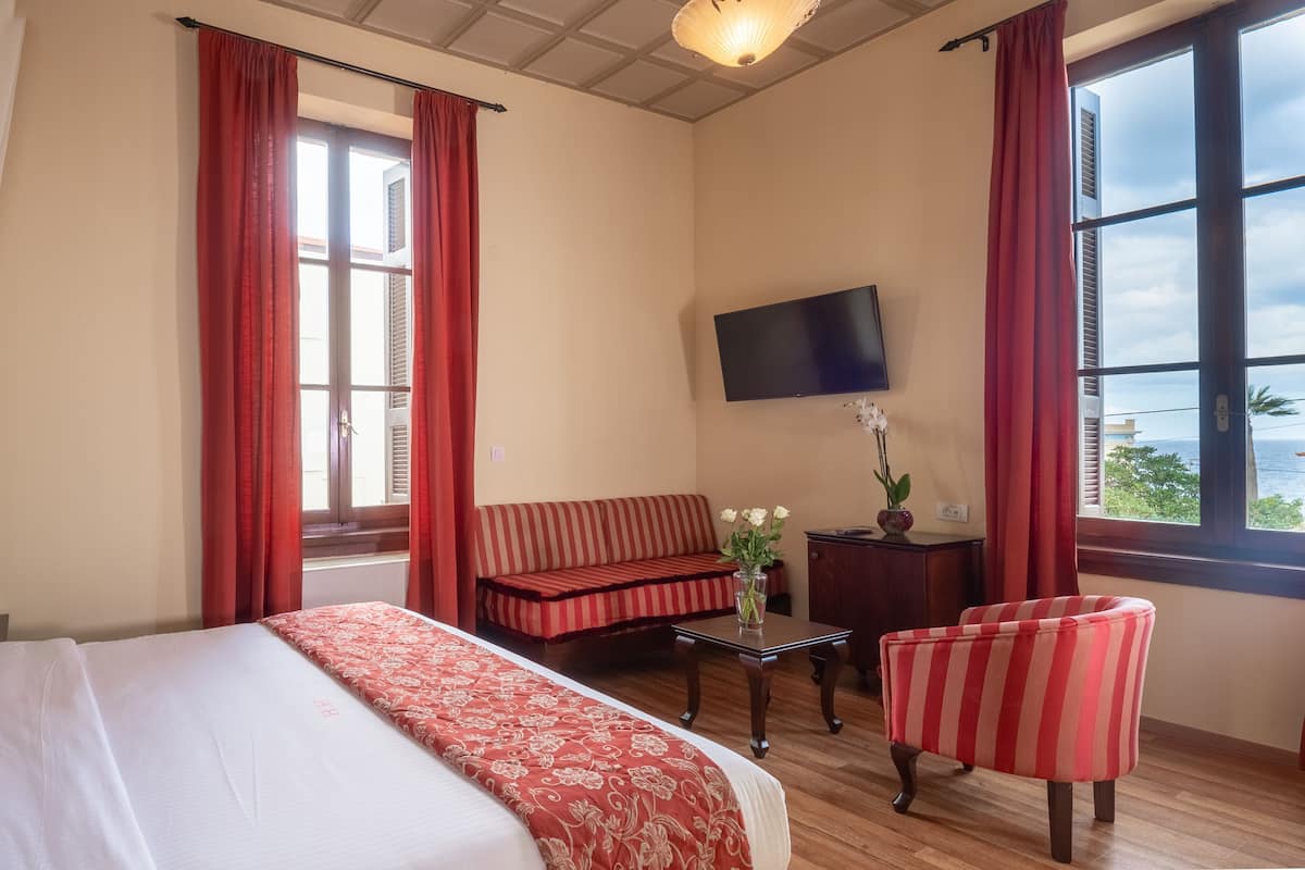 Quarto de hotel com cama, sofá, televisão e janela com cortinas.