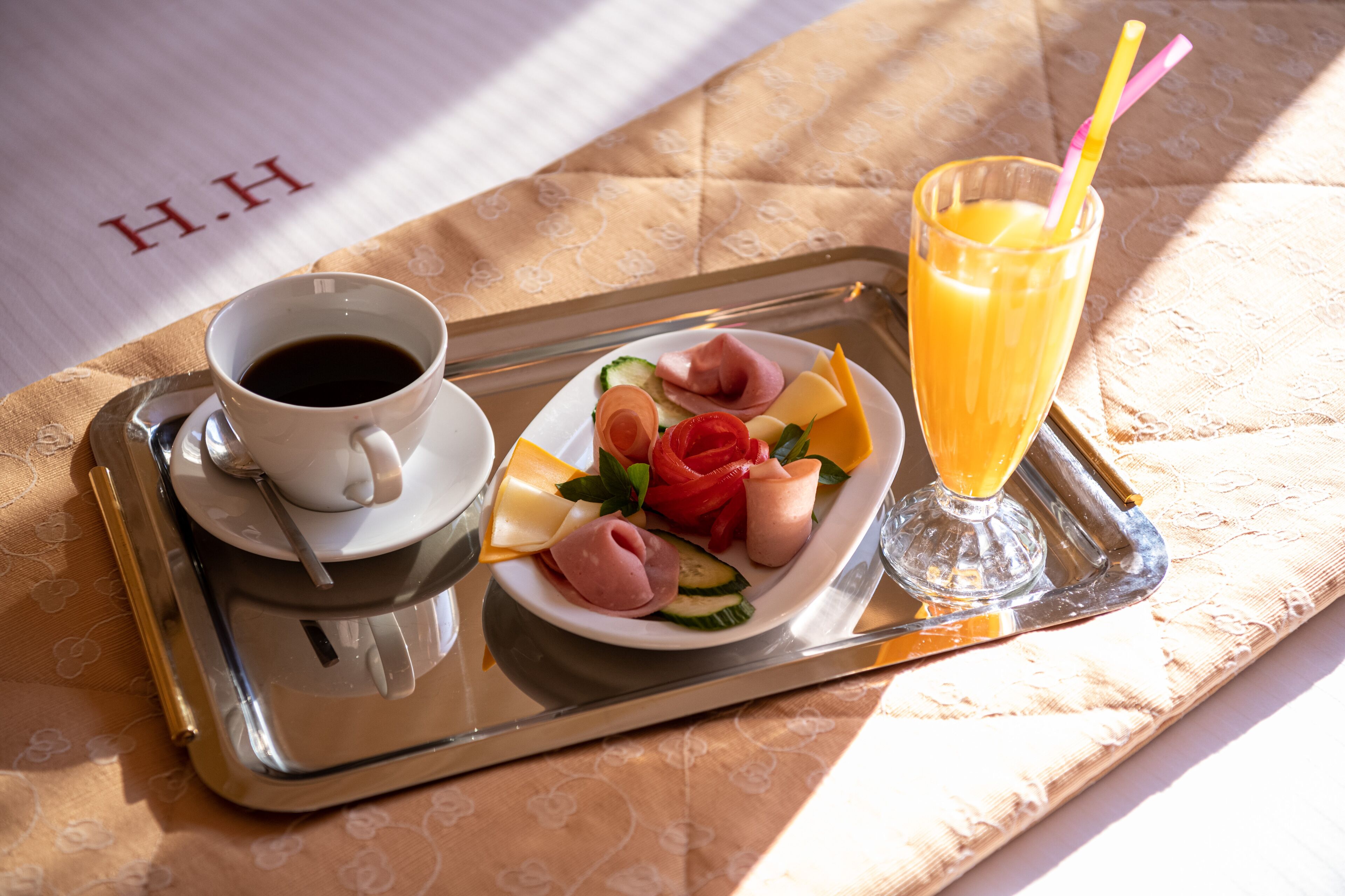 Uma bandeja com uma xícara de café, um copo de suco de laranja e um prato de comida que inclui queijo, presunto e legumes.
