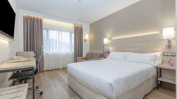 Quarto de hotel com cama, escrivaninha, cadeira e televisão.