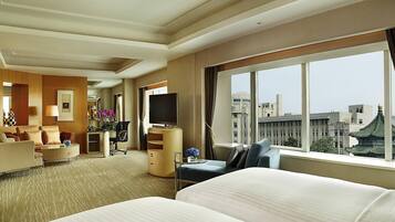 Quarto de hotel com uma cama grande, uma mesa, uma cadeira, uma televisão e vista para a cidade.