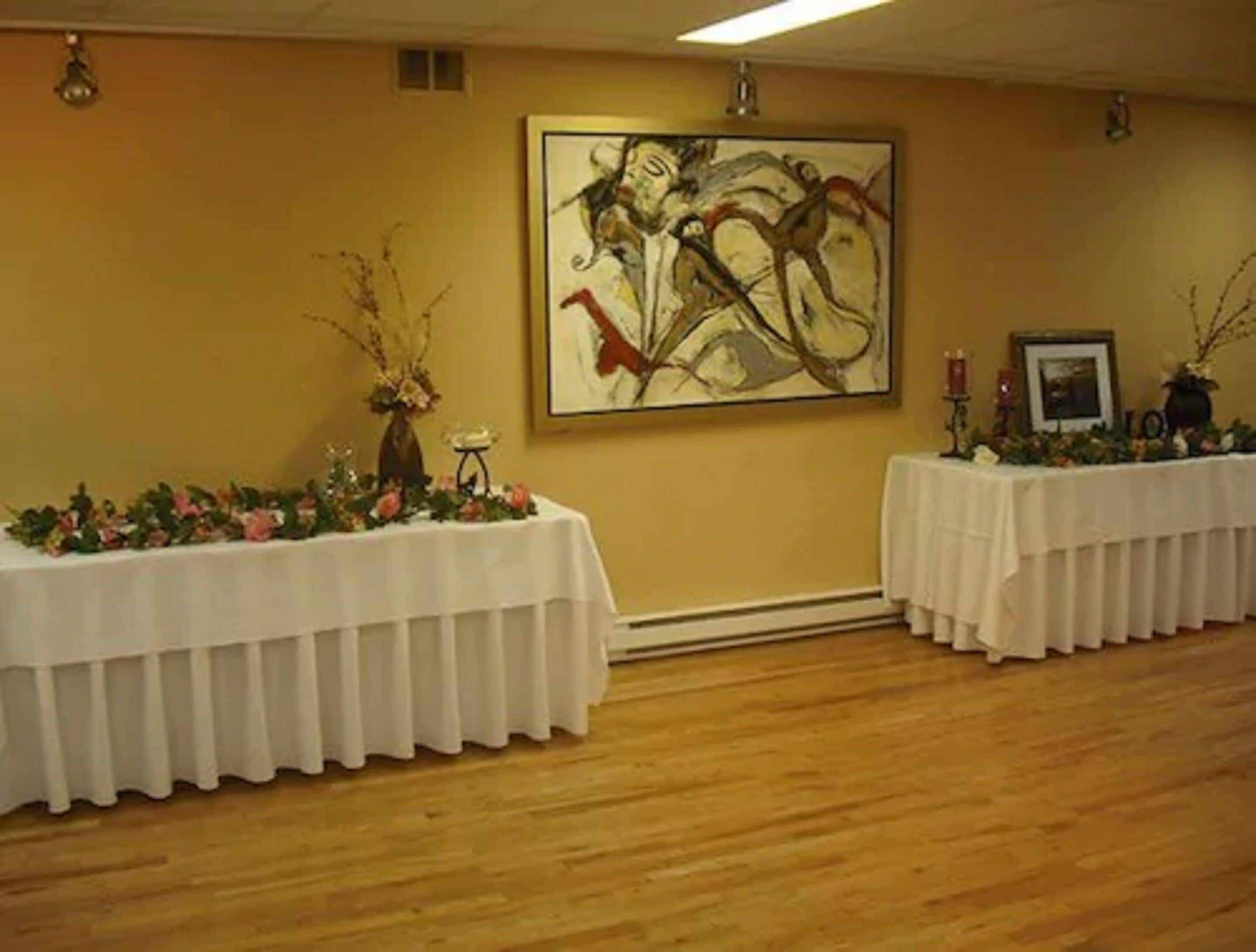 Um salão com duas mesas montadas para um evento, decorado com flores e velas.