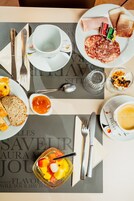 Disposição de mesa para café da manhã, com pratos de comida, talheres e cardápio.