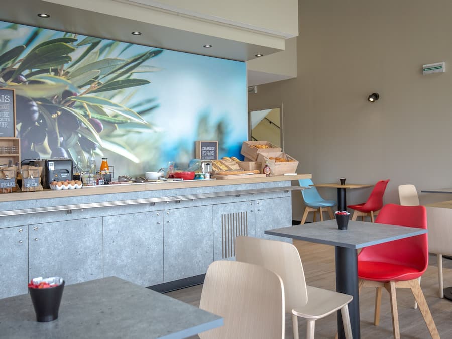Um café moderno com um balcão exibindo doces e bebidas, área de estar com mesas e cadeiras, e um grande mural na parede.