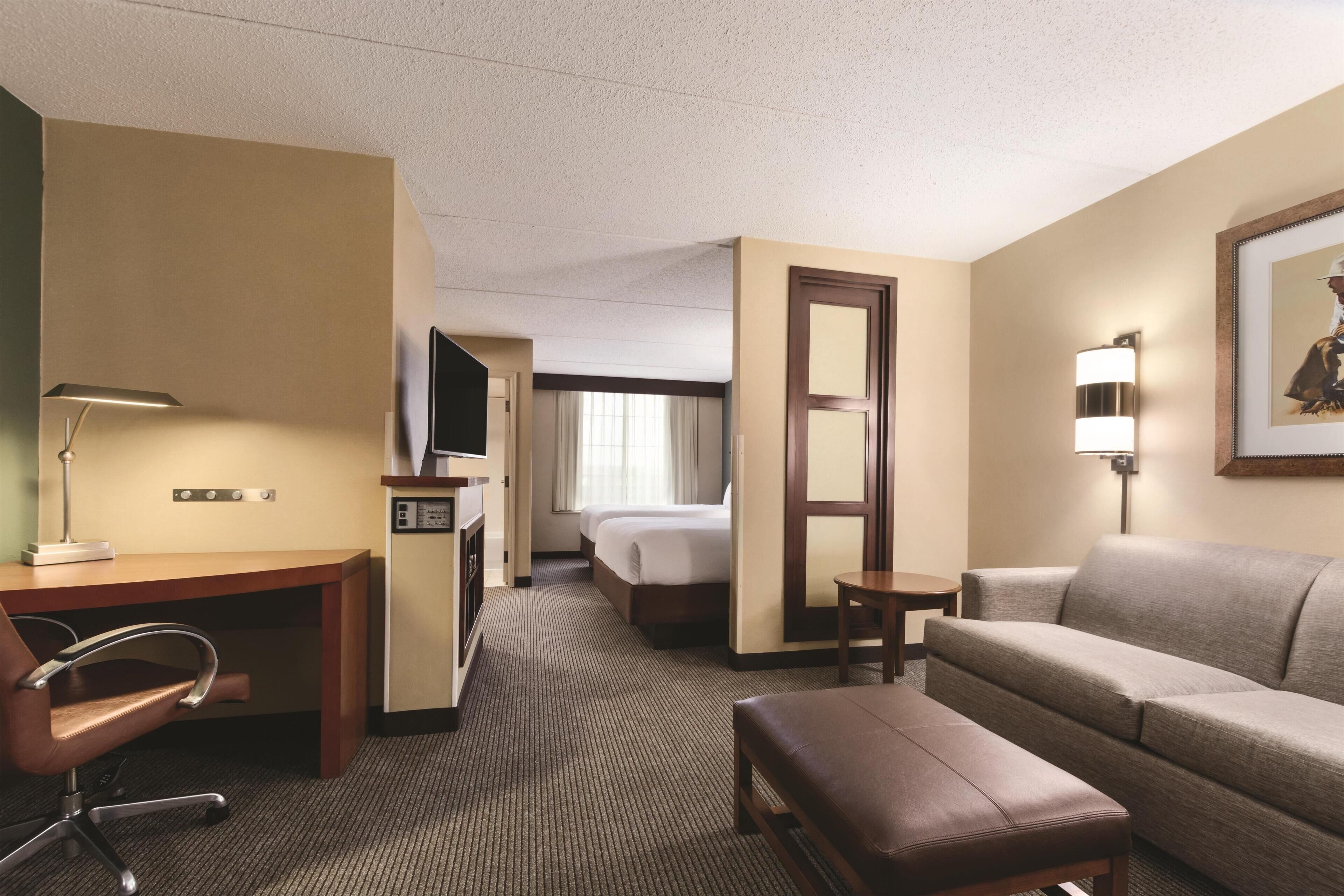 Quarto de hotel com escrivaninha, cadeira, sofá e televisão.