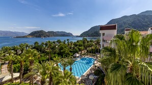 Resort com piscina rodeada por palmeiras, com vista para um corpo de água e montanhas.