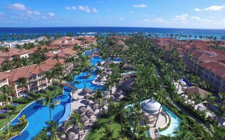 Resort com várias piscinas, palmeiras e vista para o oceano.