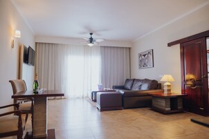 Uma sala de estar moderna com um sofá, uma mesa de jantar com cadeiras, uma televisão, um ventilador de teto e uma porta.