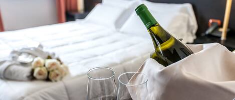 Quarto de hotel com uma cama bem arrumada, uma garrafa de vinho e duas taças de vinho vazias sobre uma bandeja.