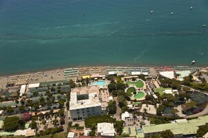 Vista aérea de um resort à beira-mar com praia, piscina e vários edifícios de hotel.