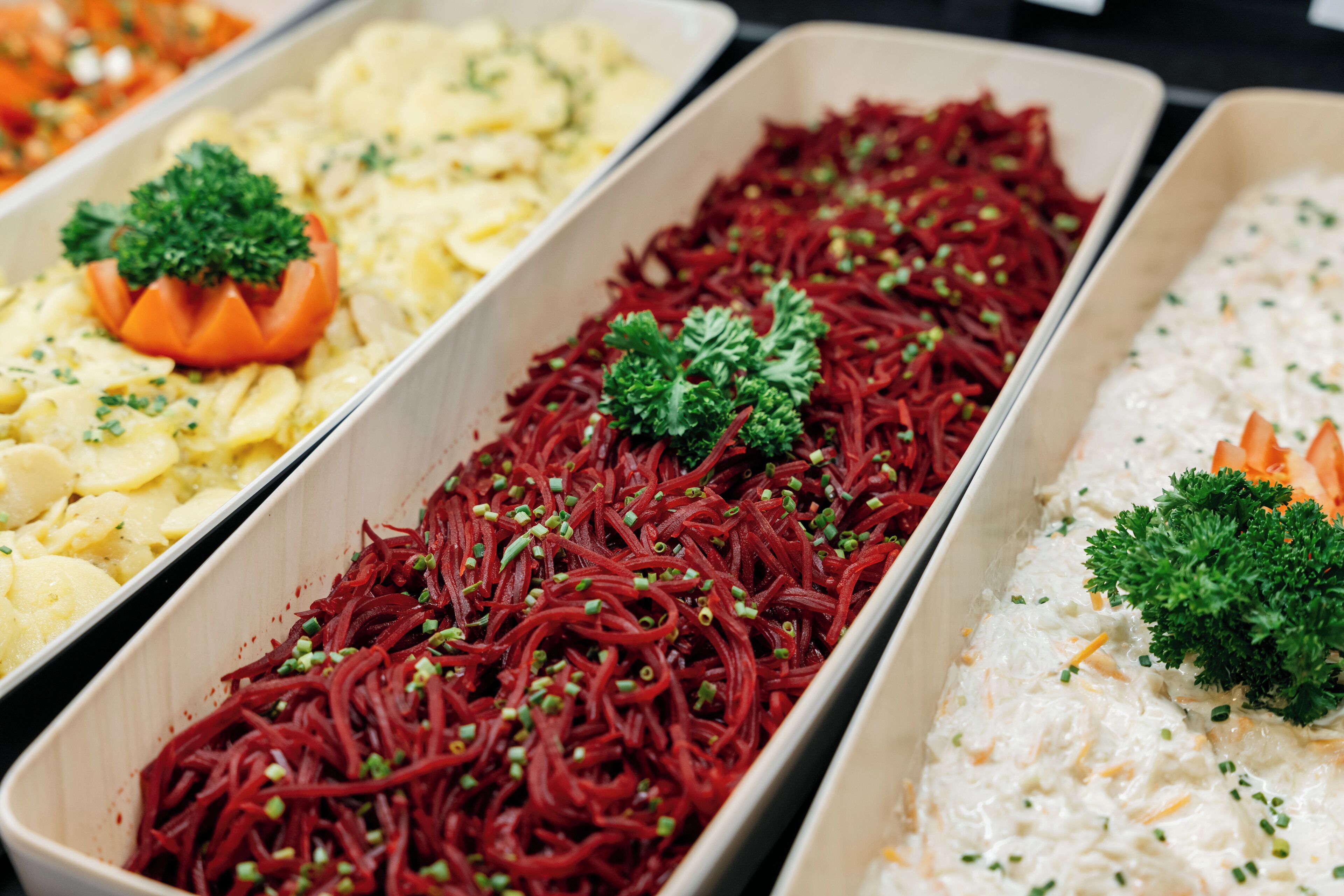 Buffet variado com diversos pratos, incluindo macarrão, batatas e um prato cremoso, cada um decorado com ervas.