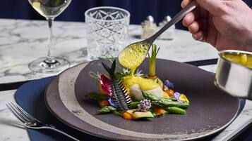 Uma mesa de jantar com um prato de comida, um garfo, um copo de vinho branco e um copo decorativo.