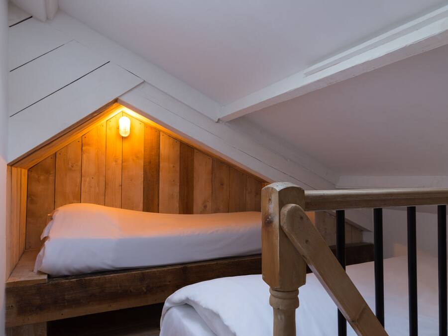 Uma cama de solteiro em um quarto estilo loft, com vigas de madeira e teto inclinado.