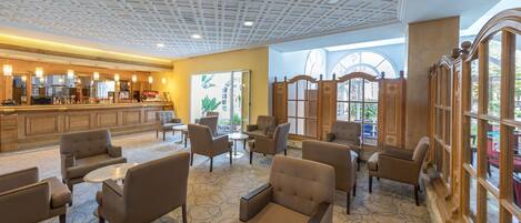 Um hall espaçoso com teto alto, área de recepção e espaço de estar com várias poltronas e uma mesa de centro.