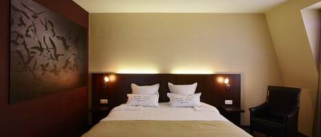 Quarto de hotel com uma cama grande, duas mesas de cabeceira, uma cadeira e uma obra de arte na parede.