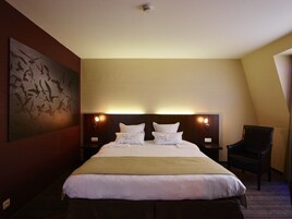 Quarto de hotel com uma cama grande, duas mesas de cabeceira, uma cadeira e uma obra de arte na parede.